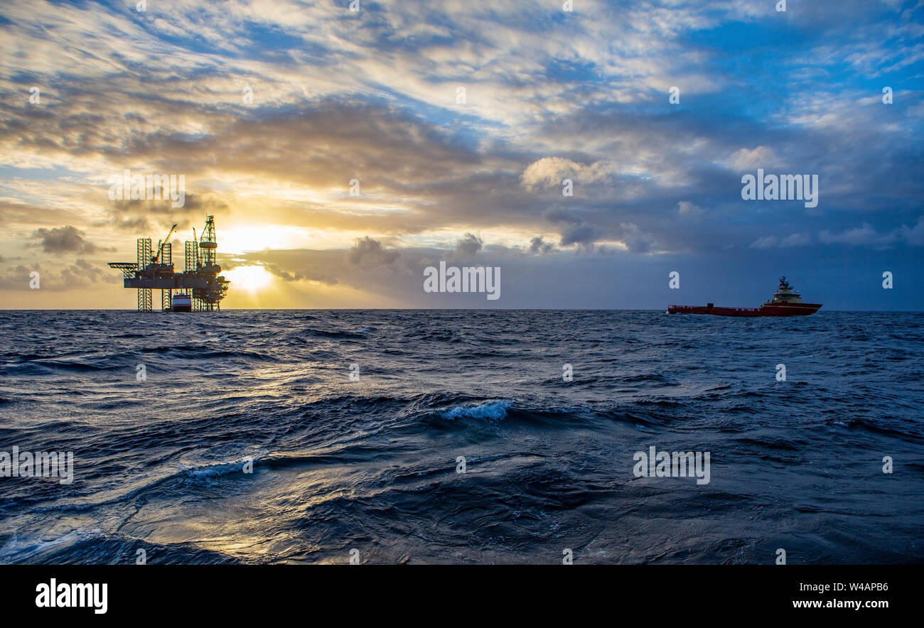 Offshore drilling platform during sunrise with work vessel Stock Photo ...