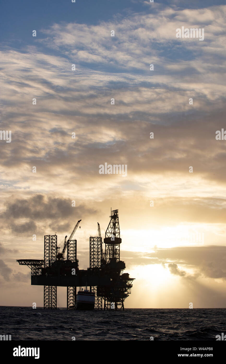 Offshore drilling platform during sunrise with work vessel Stock Photo ...
