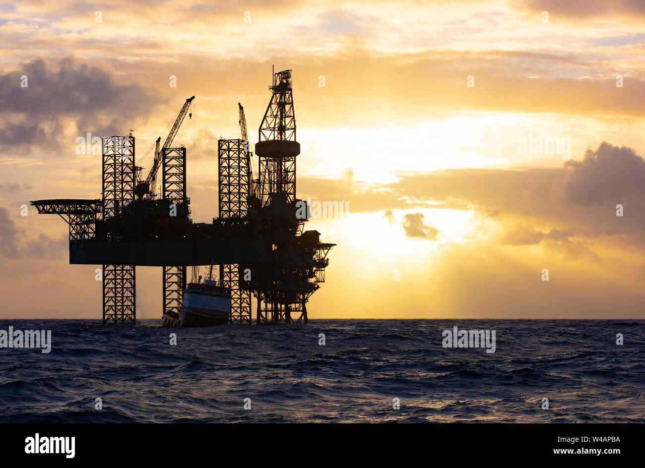Offshore drilling platform during sunrise with work vessel Stock Photo ...