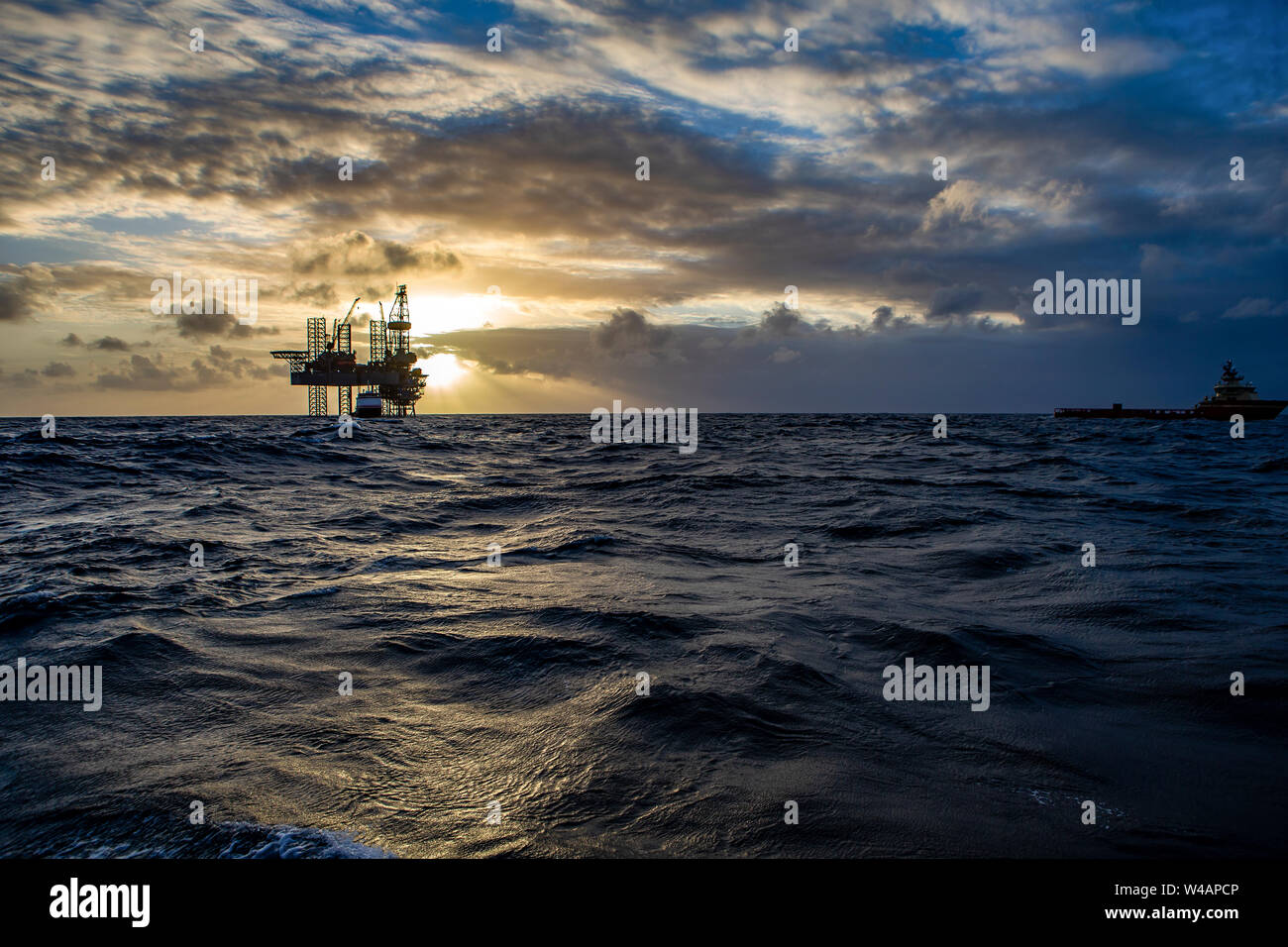 Offshore drilling platform during sunrise with work vessel Stock Photo ...