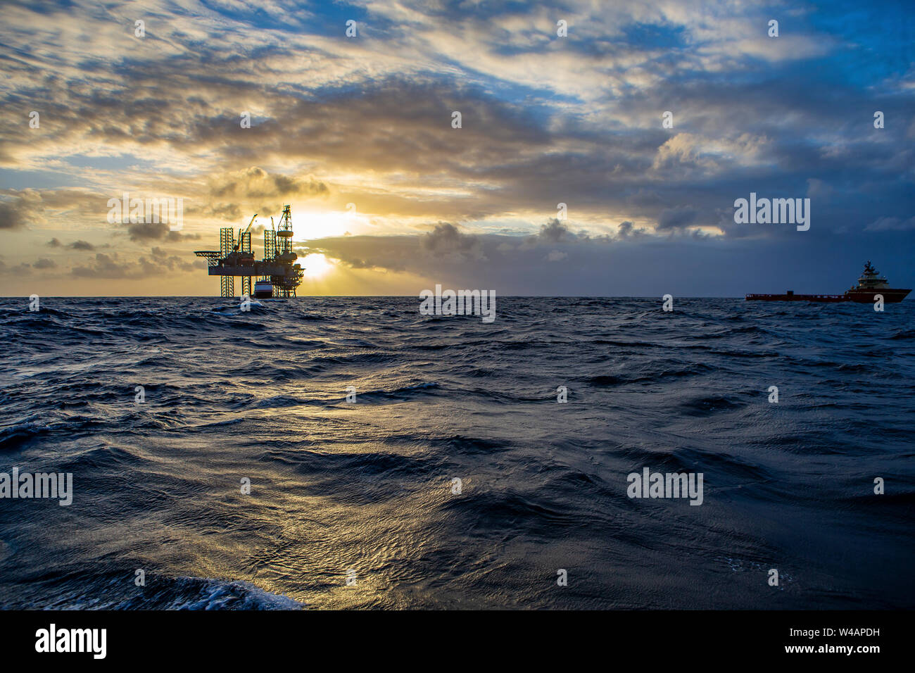 Offshore drilling platform during sunrise with work vessel Stock Photo ...