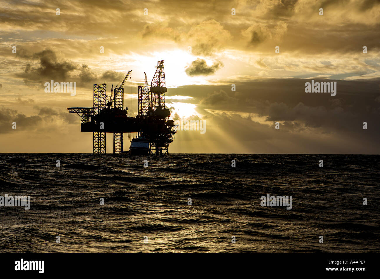 Offshore drilling platform during sunrise with work vessel Stock Photo ...