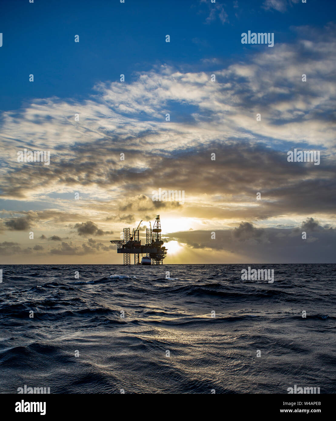 Offshore drilling platform during sunrise with work vessel Stock Photo ...