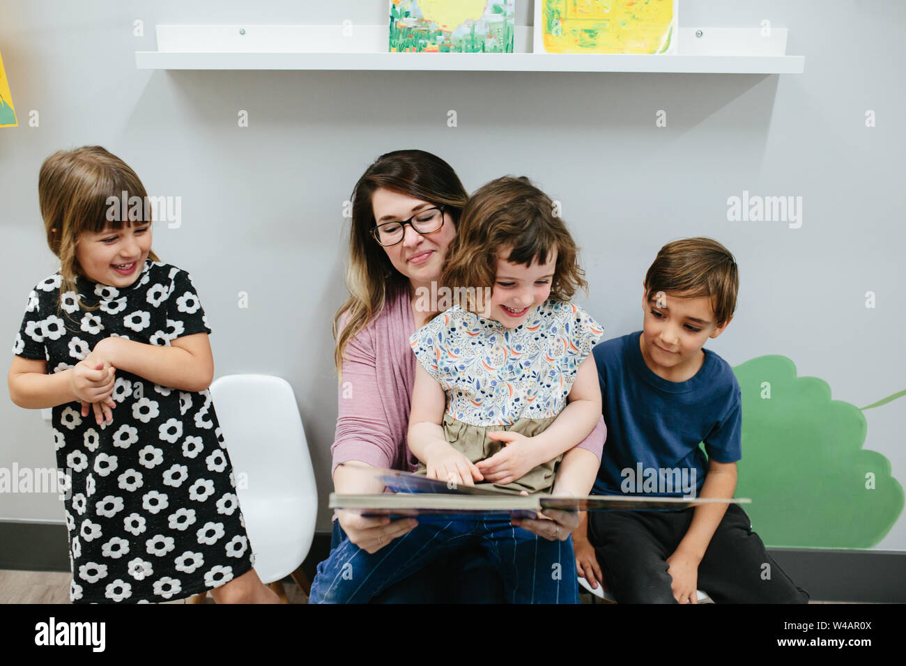 Teacher reads a book to three happy students while one sits on her lap ...
