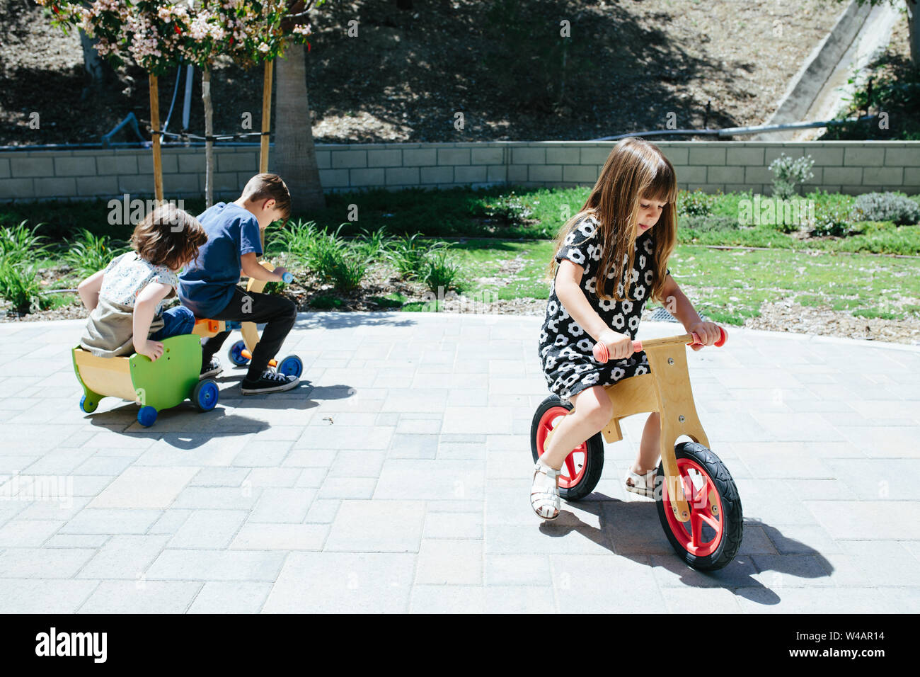 Three kids outside ride around on wooden bicycles Stock Photo - Alamy