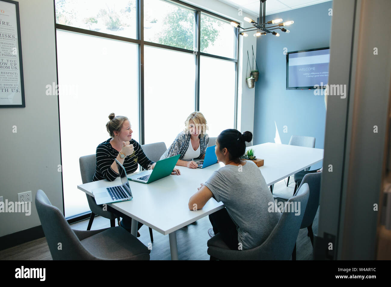Three women sit at a conference table and have a discussion Stock Photo ...