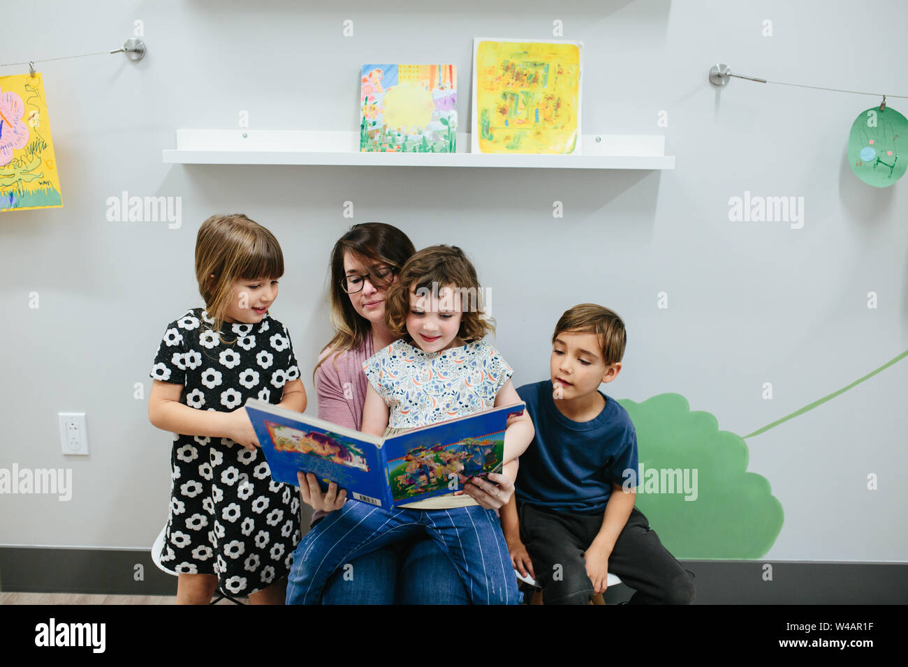 Teacher and three students read a book together Stock Photo - Alamy