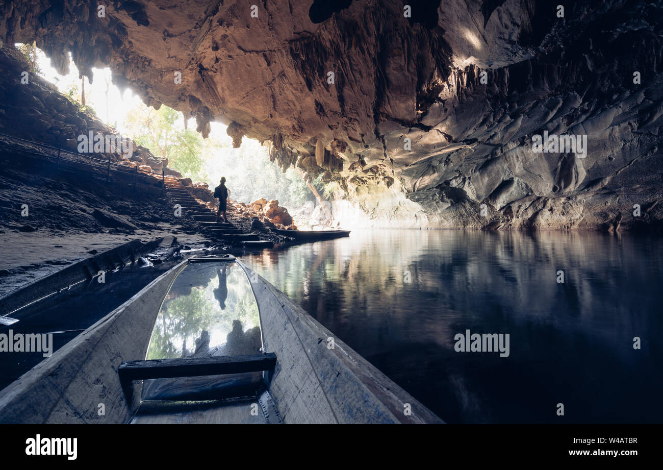 Human silhouette stands inside water cave with torch in hand in Konglor ...