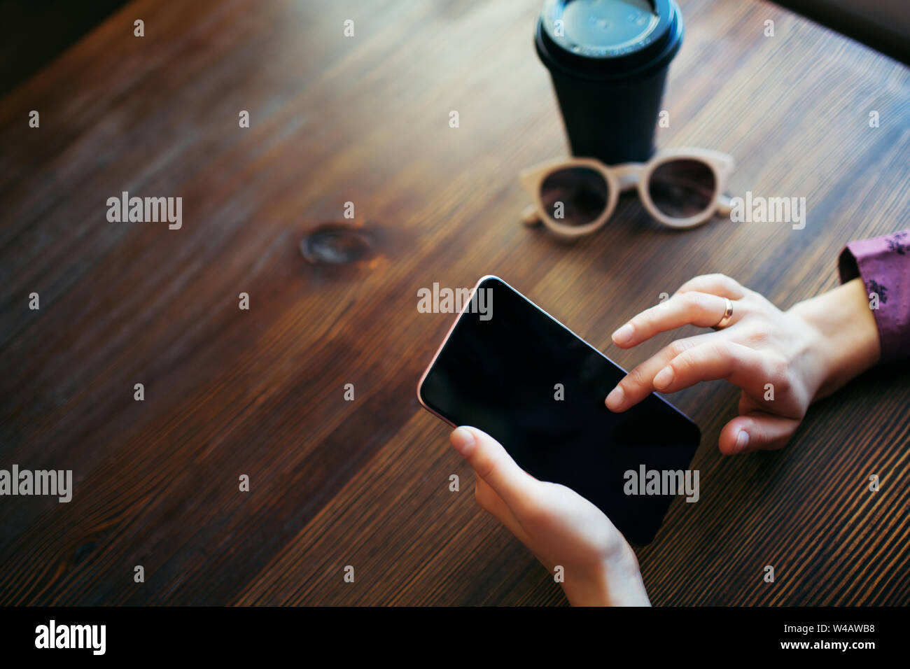 Overview of female hands, scrolling the screen of mobile phone. A cup ...