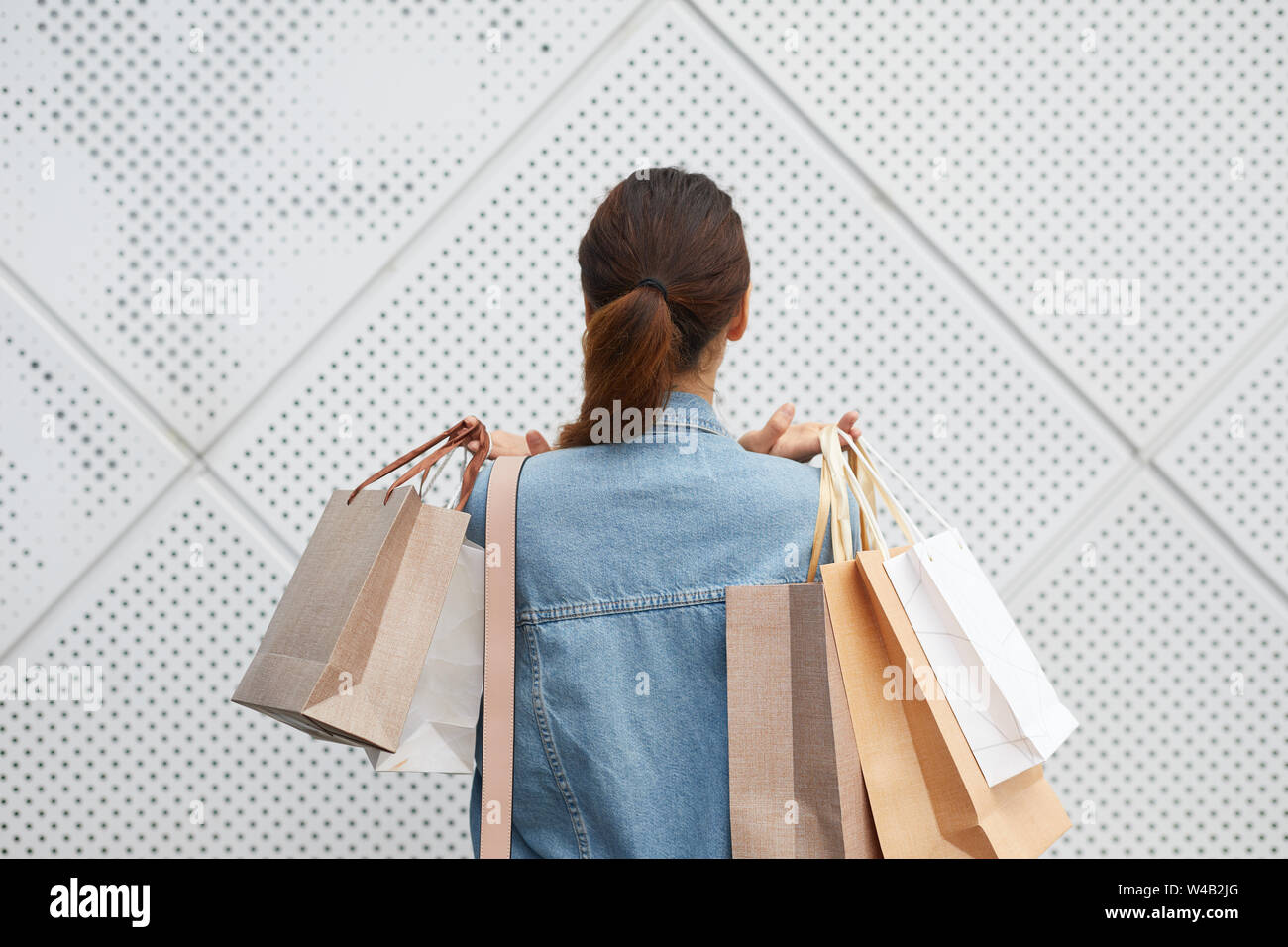Rear view of young lady with pony tail standing against tiled wall and ...