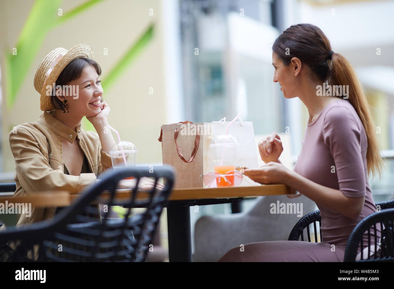 Happy fashionable young ladies sitting at round table on food court and ...