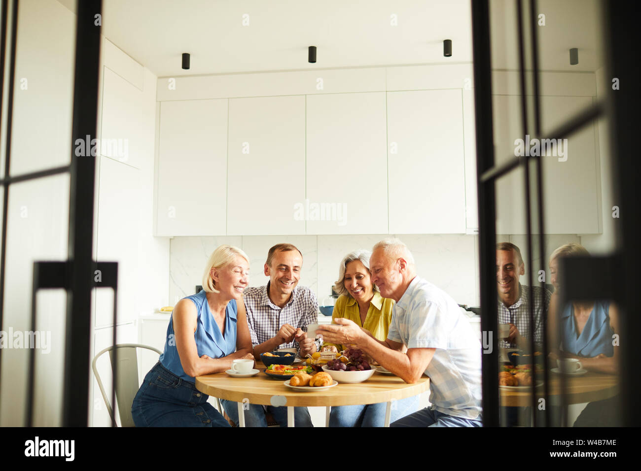 Group of cheerful senior people sitting around table in kitchen shot ...