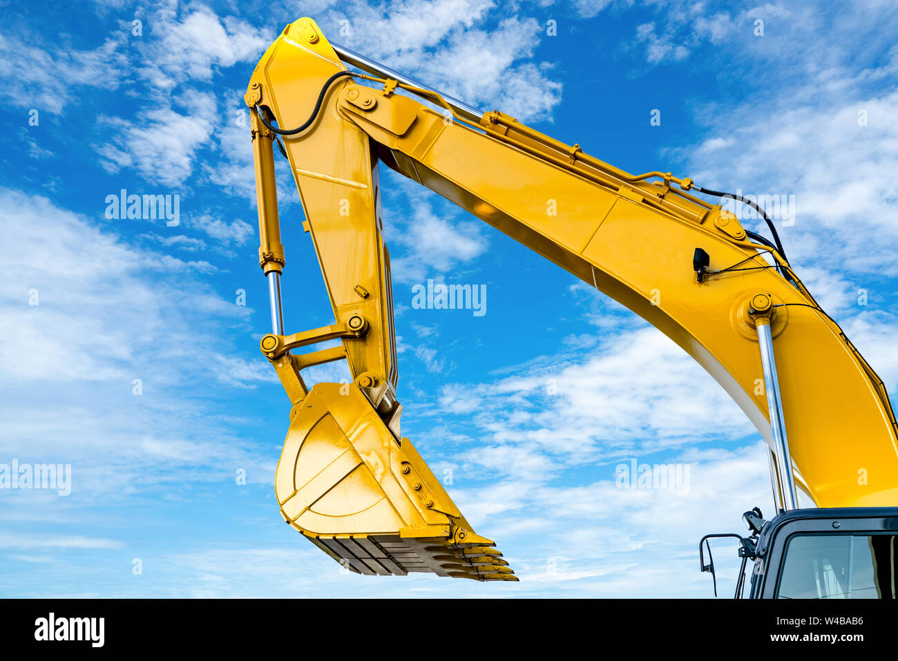 Yellow backhoe with hydraulic piston arm against blue sky. Heavy ...