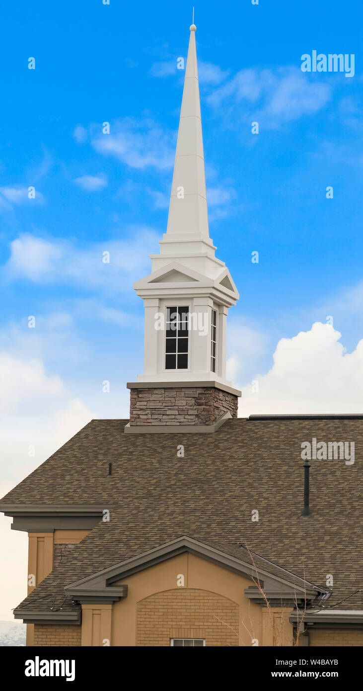 Vertical tall White steeple on top of the pitched roof of a church with ...