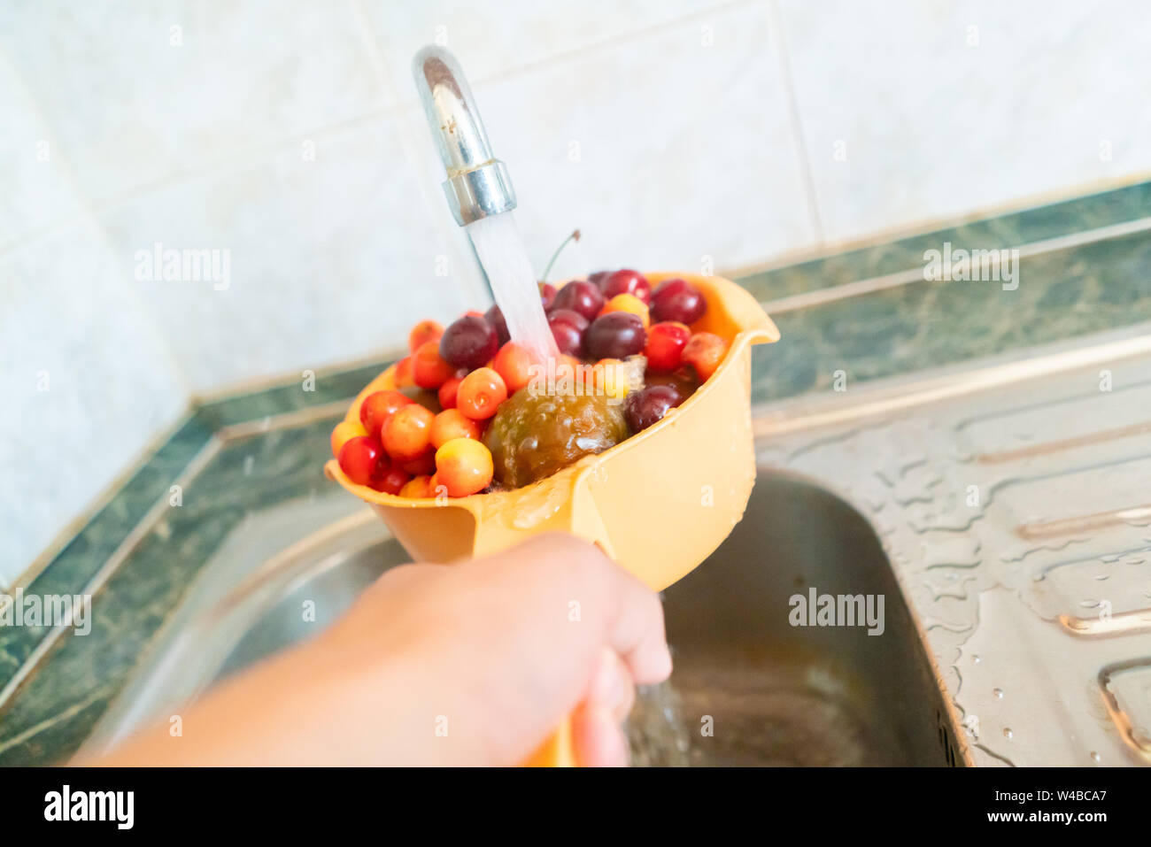 hand holding a colander with fresh fruit and berries and washing it in ...