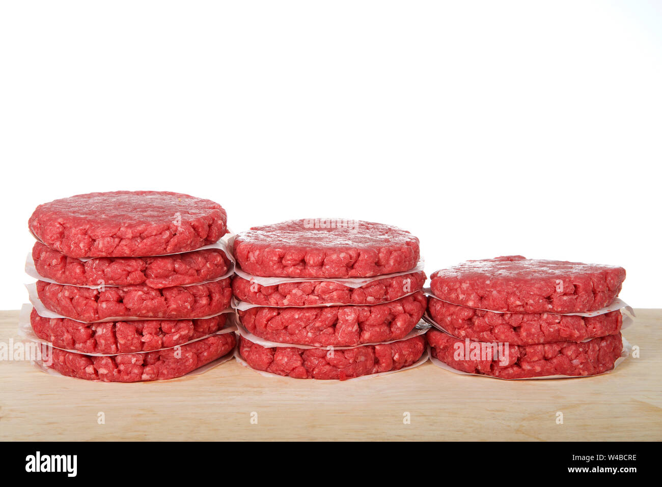 Stacks of raw hamburger meat patties on a wood table with pieces of ...