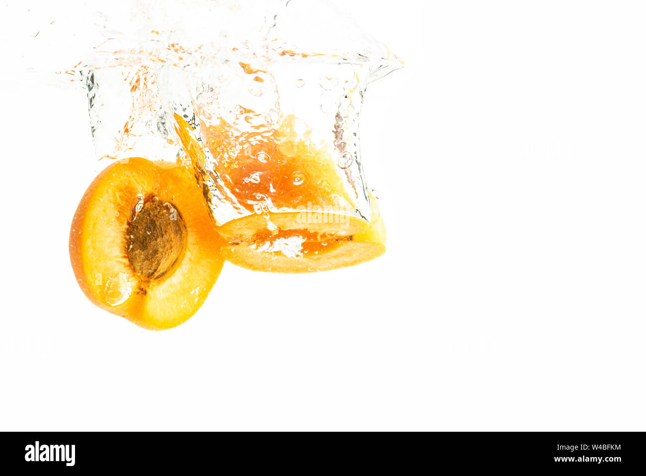 Fresh ripe apricot split in half falling in the clear water, isolated ...