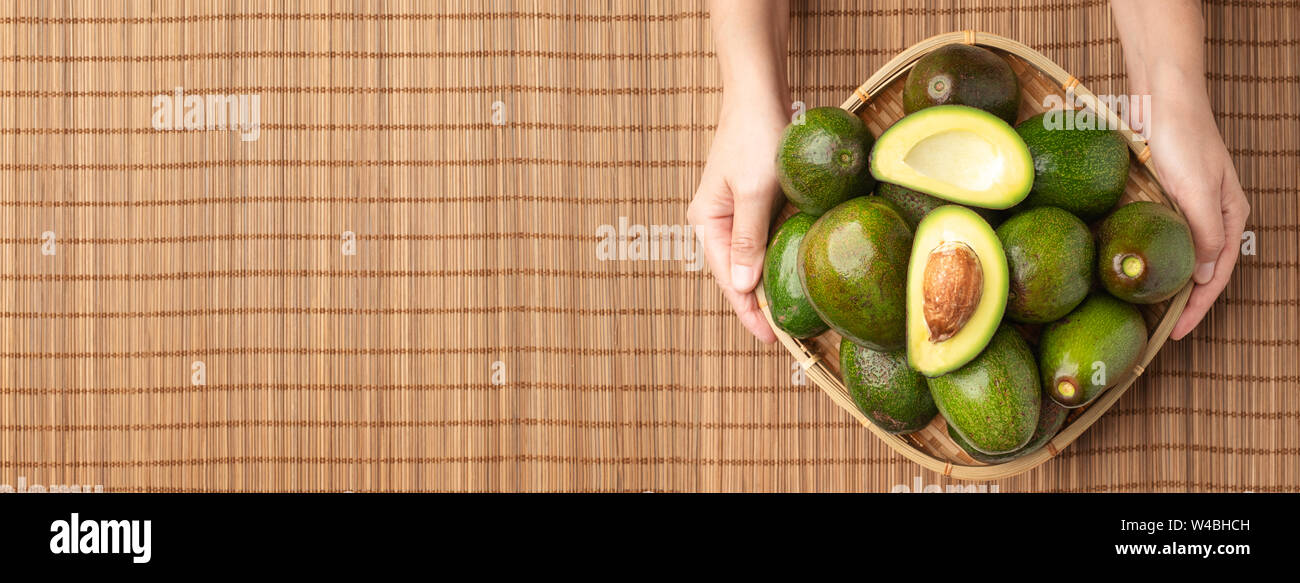 Hand holding organic avocados half cut with seed and whole fruit in ...