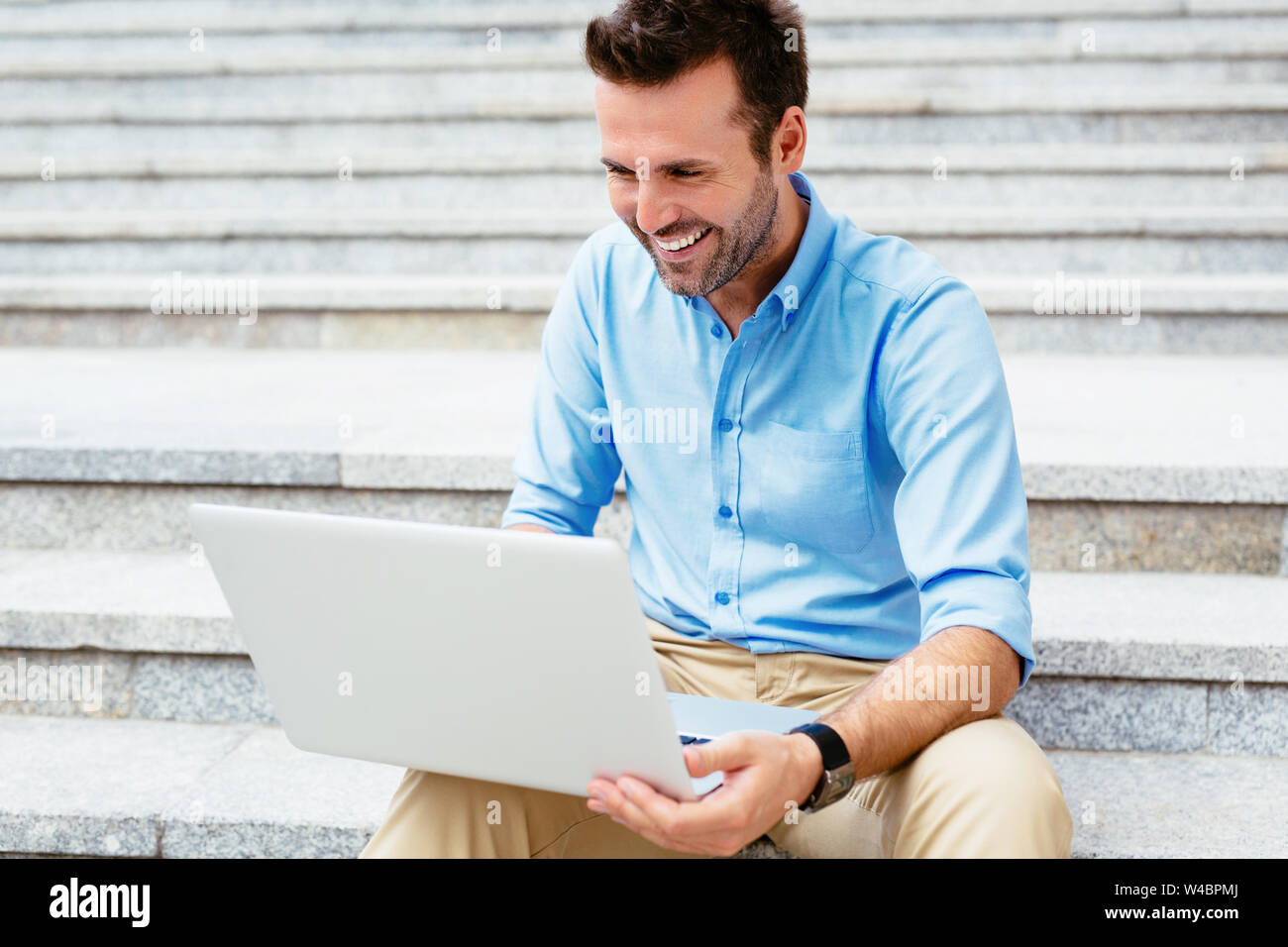 Happy student browsing the internet on his laptop and sitting outdoor ...