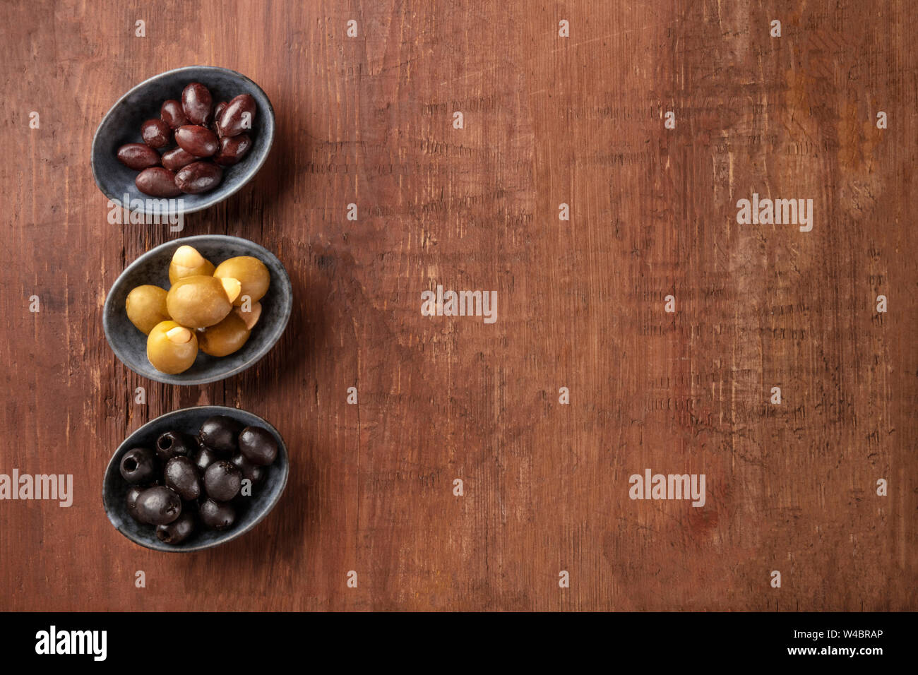 Various types of olives in bowls on a dark rustic wooden background ...