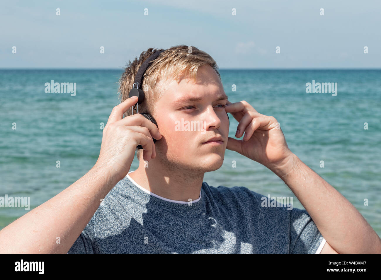Portrait of a young man on the beach listening to music on headphones ...