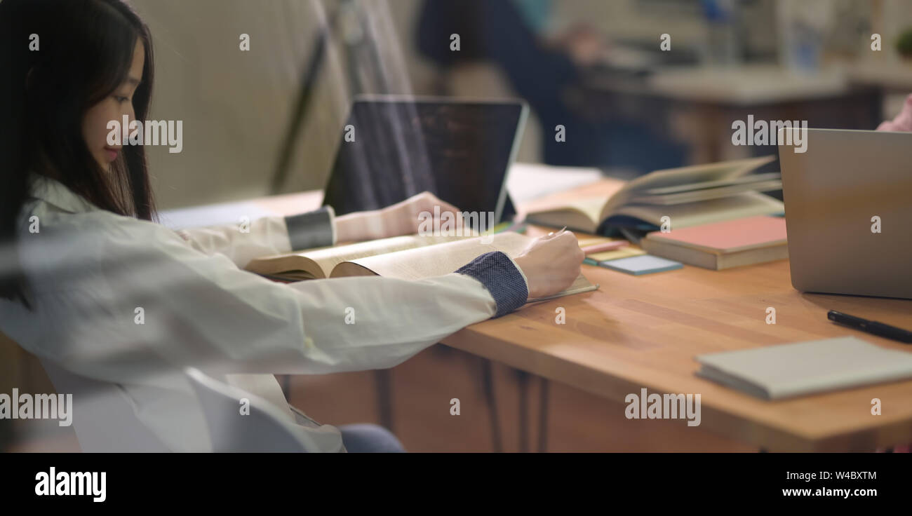Beautiful young college student reading for exam in library with laptop ...