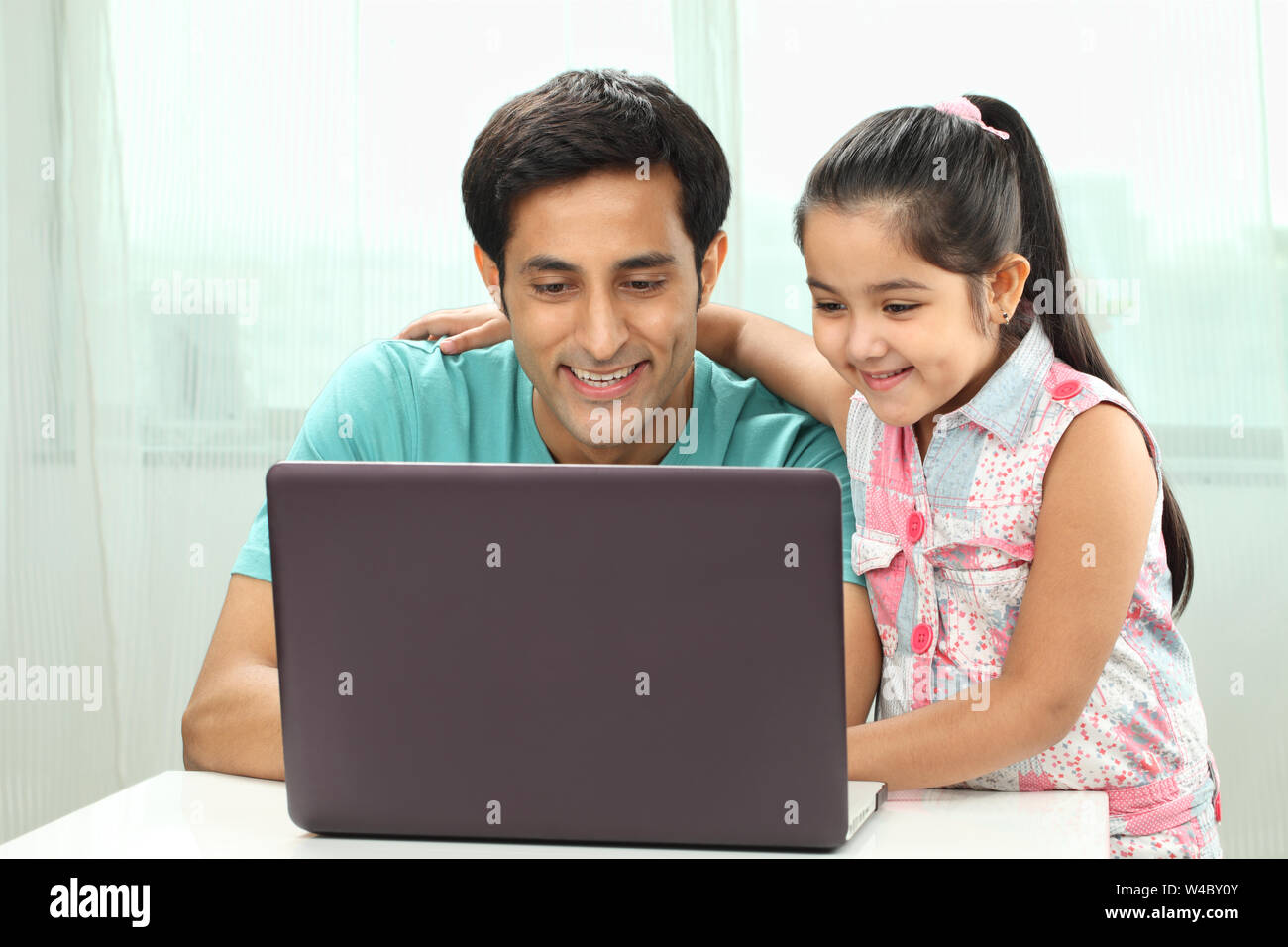 Man assisting his daughter in using a laptop Stock Photo - Alamy