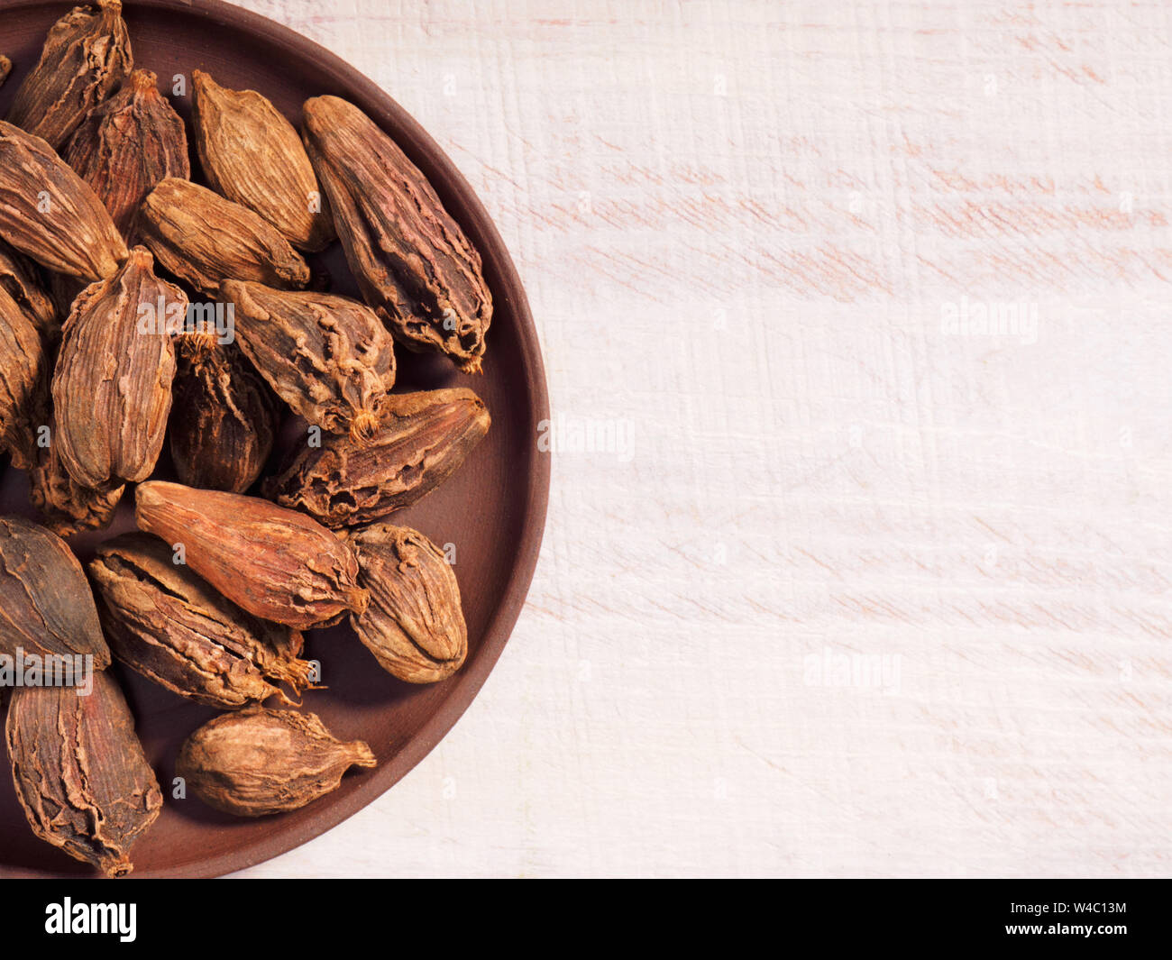 Black cardamom (Amomum subulatum) on a brown clay plate on a wooden ...