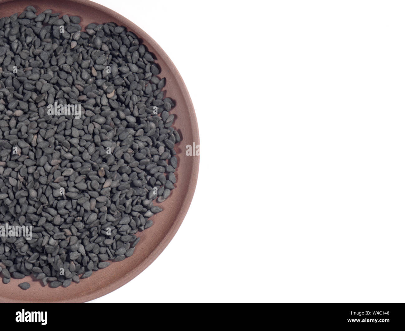 Black sesame (Sesamum) in brown clay plate on white background with ...