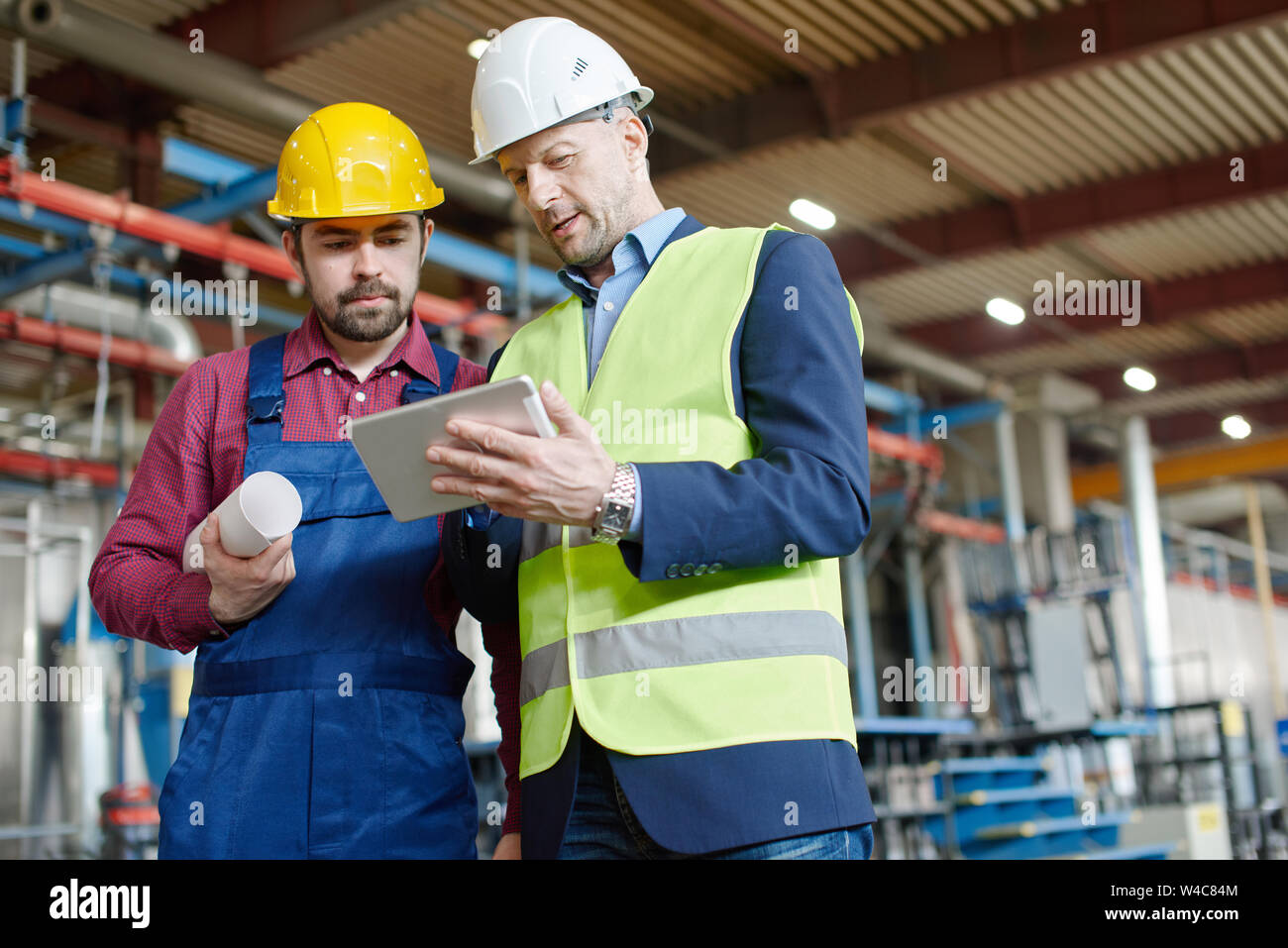 Engineers in hard hats looking at the screen of a tablet Stock Photo ...