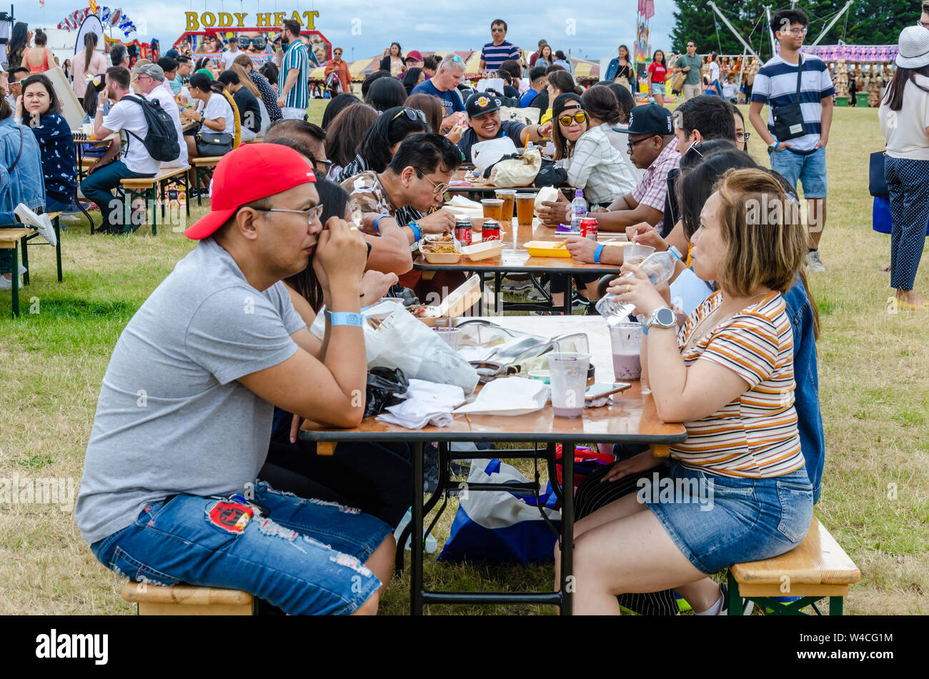 People sit outside at trestle table and eat street food purchased form ...