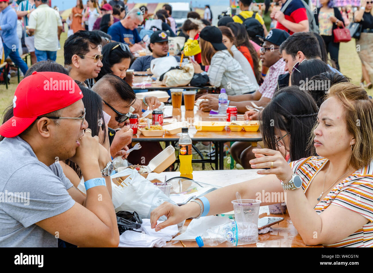 People sit outside at trestle table and eat street food purchased form ...