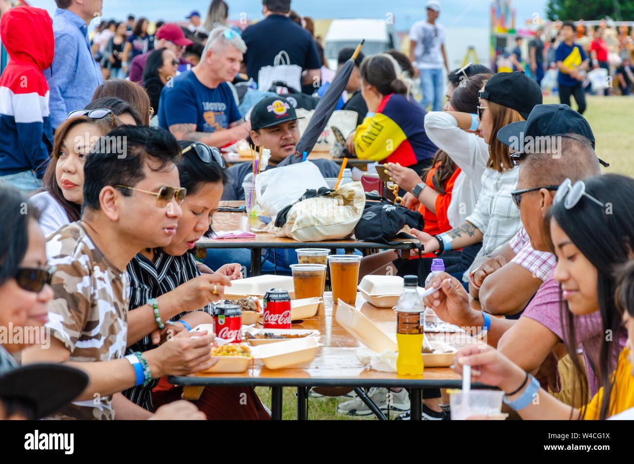 People sit outside at trestle table and eat street food purchased form ...