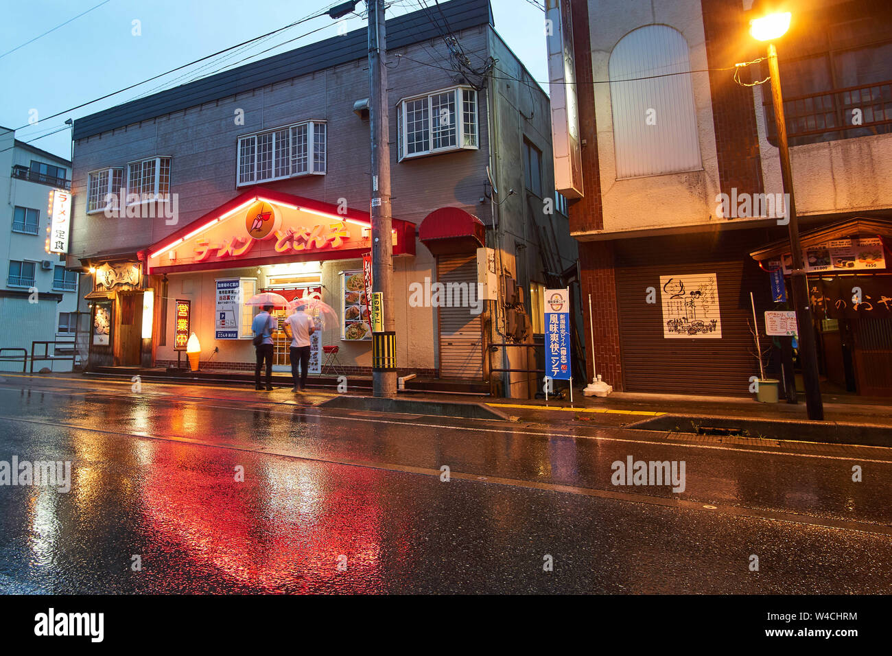Two men with umbrellas stand outside of a Dosanko Ramen restaurant in ...