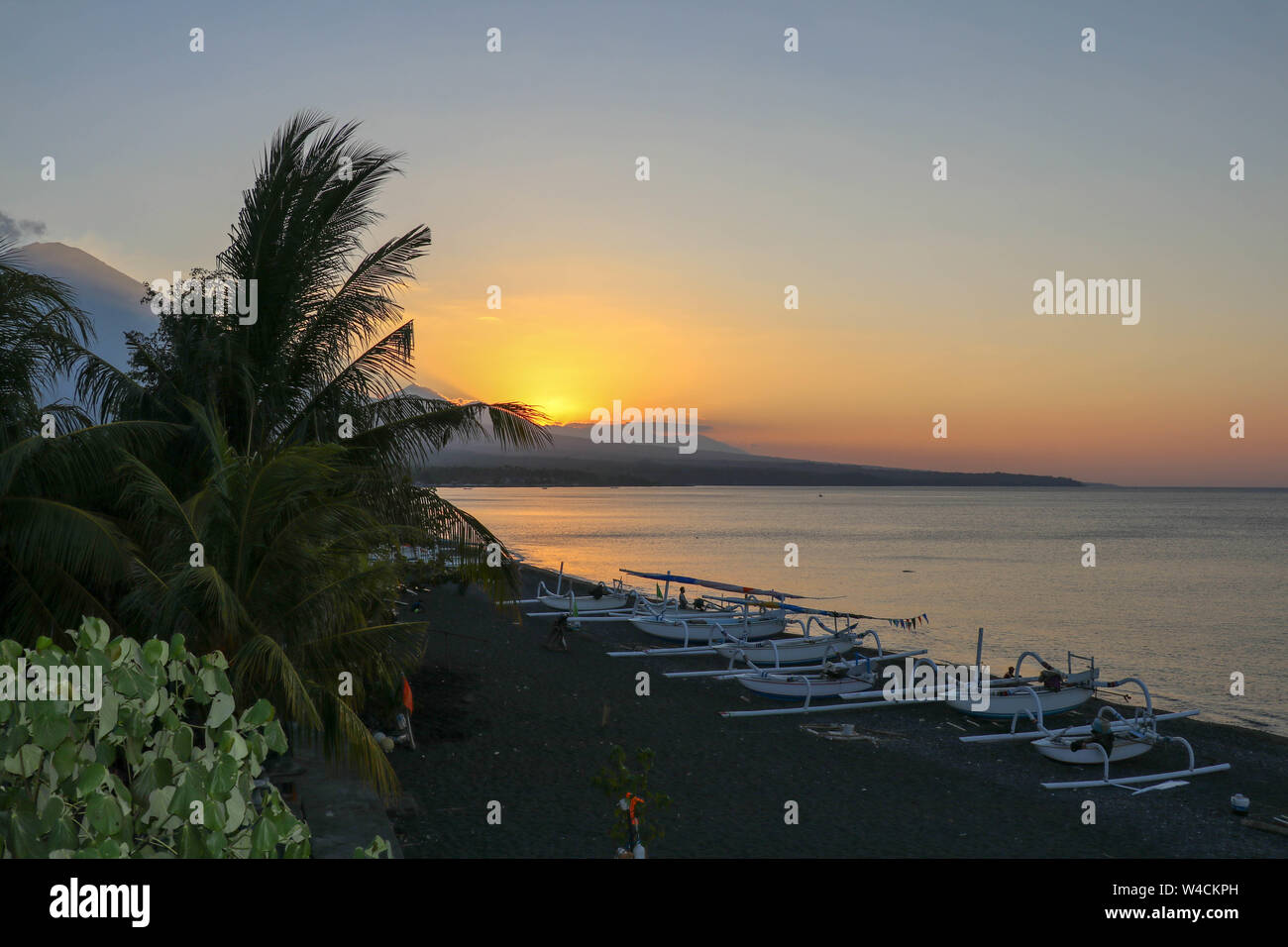 The sun set behind a mountain range near the active volcano on Bali ...