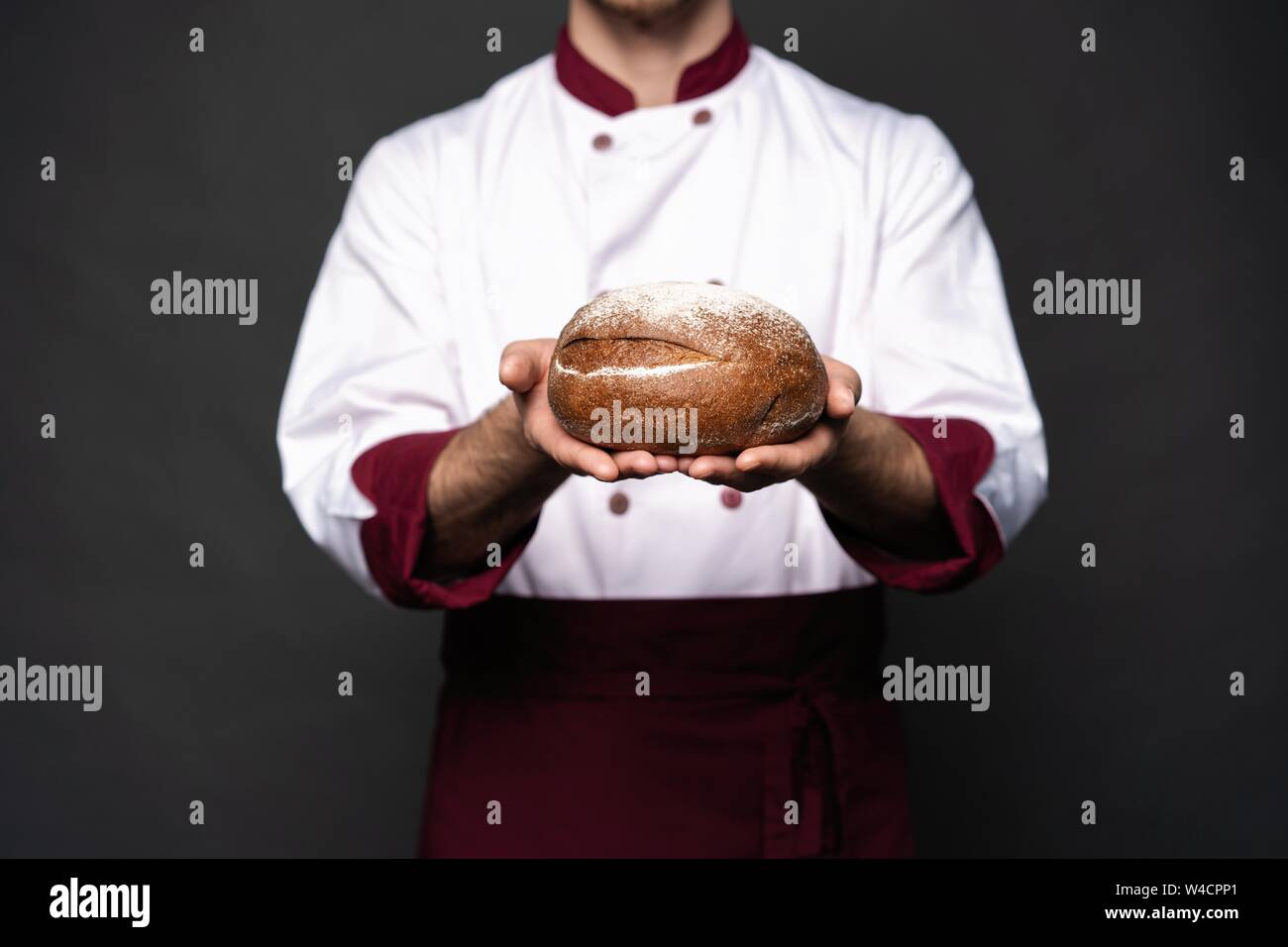 Male baker holding bread loaf and looking at camera isolated on black ...