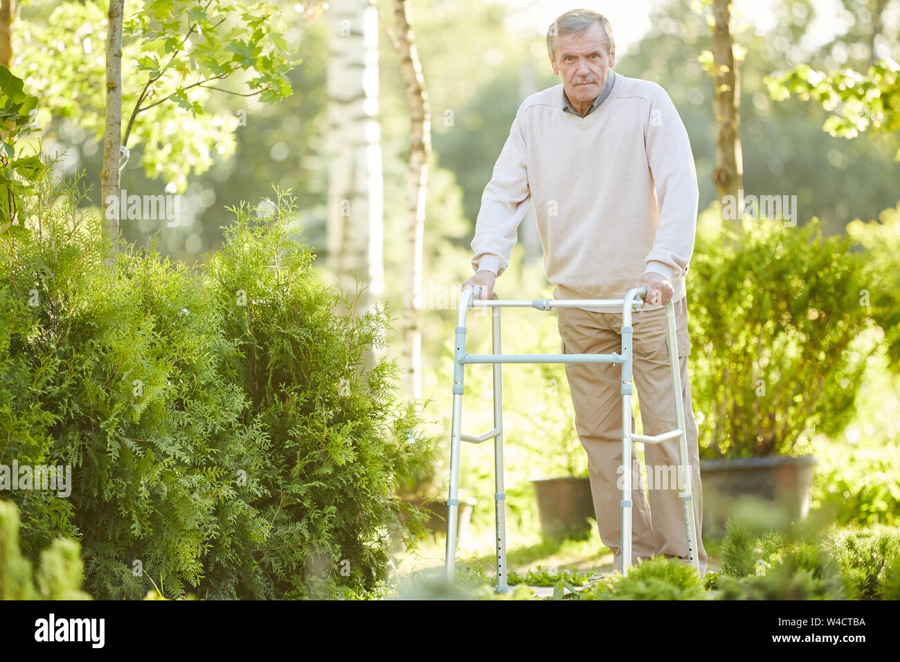 Full length portrait of senior man leaning on walker posing outdoors in ...