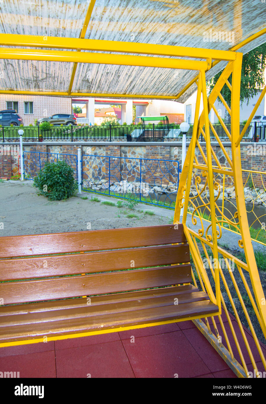 City Park in summer, empty wooden swing with yellow decorative metal ...