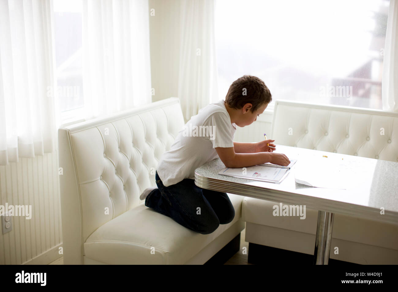 Young boy kneeling at a dining table doing his homework Stock Photo - Alamy