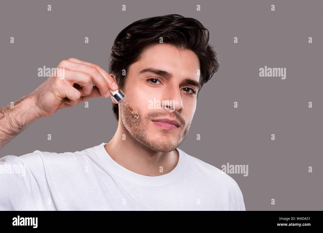 Young man applying organic essential serum on face Stock Photo - Alamy