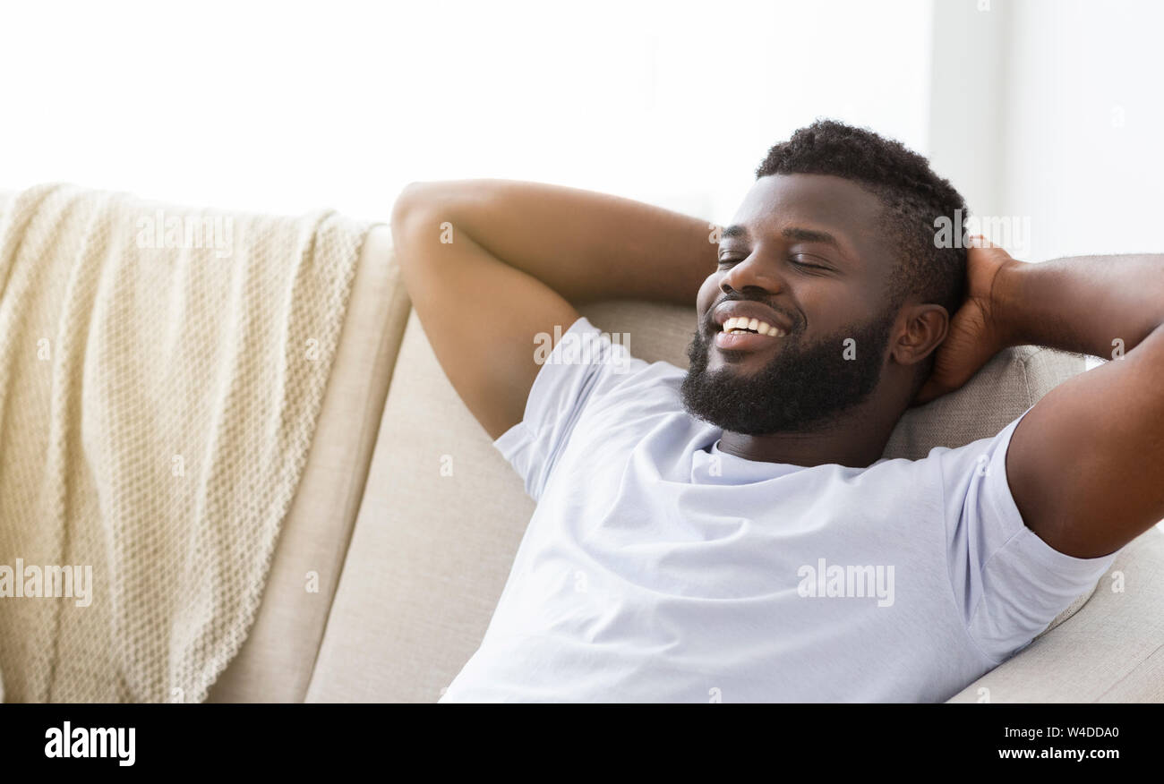 Cheerful black guy resting on sofa with closed eyes Stock Photo - Alamy