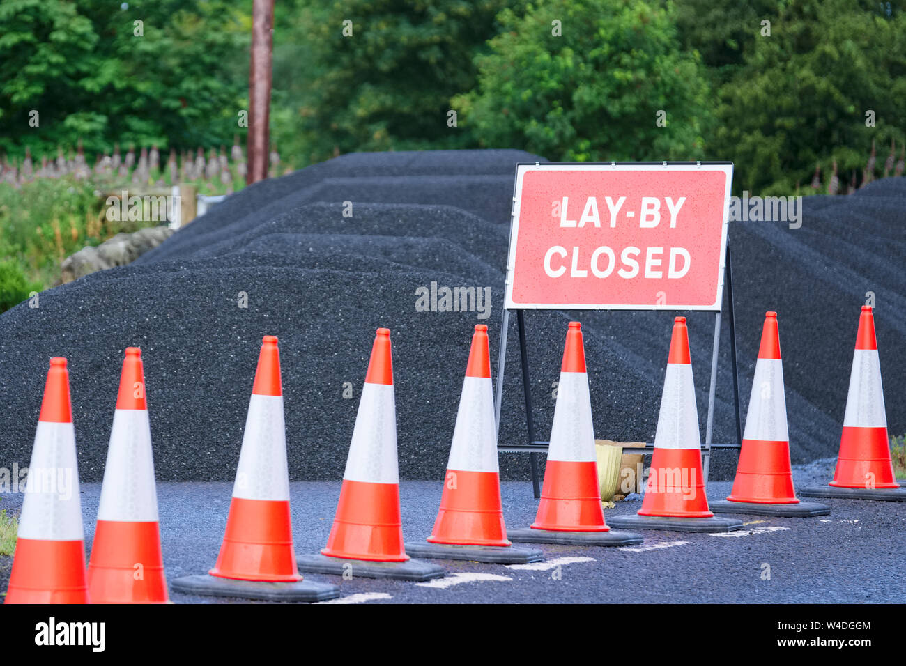 Road lay by closed sign with pile of black tar and red traffic cones ...