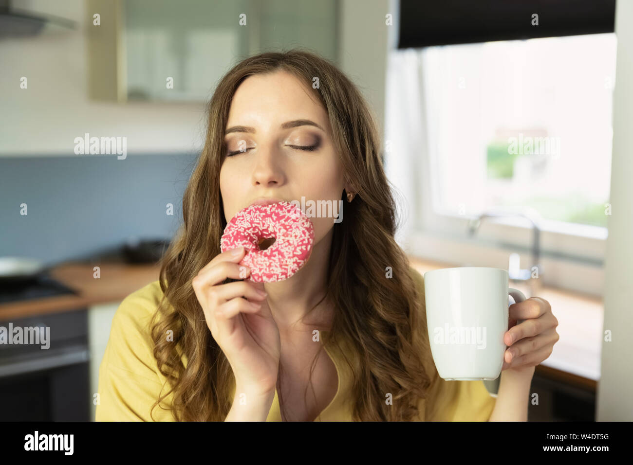 Young beautiful girl is having breakfast at home in the kitchen. She ...