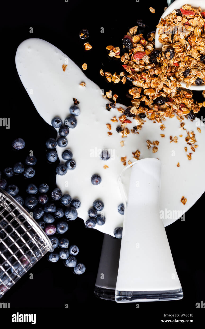 Yogurt spilled from glass pitcher, blueberries poured from steel ...