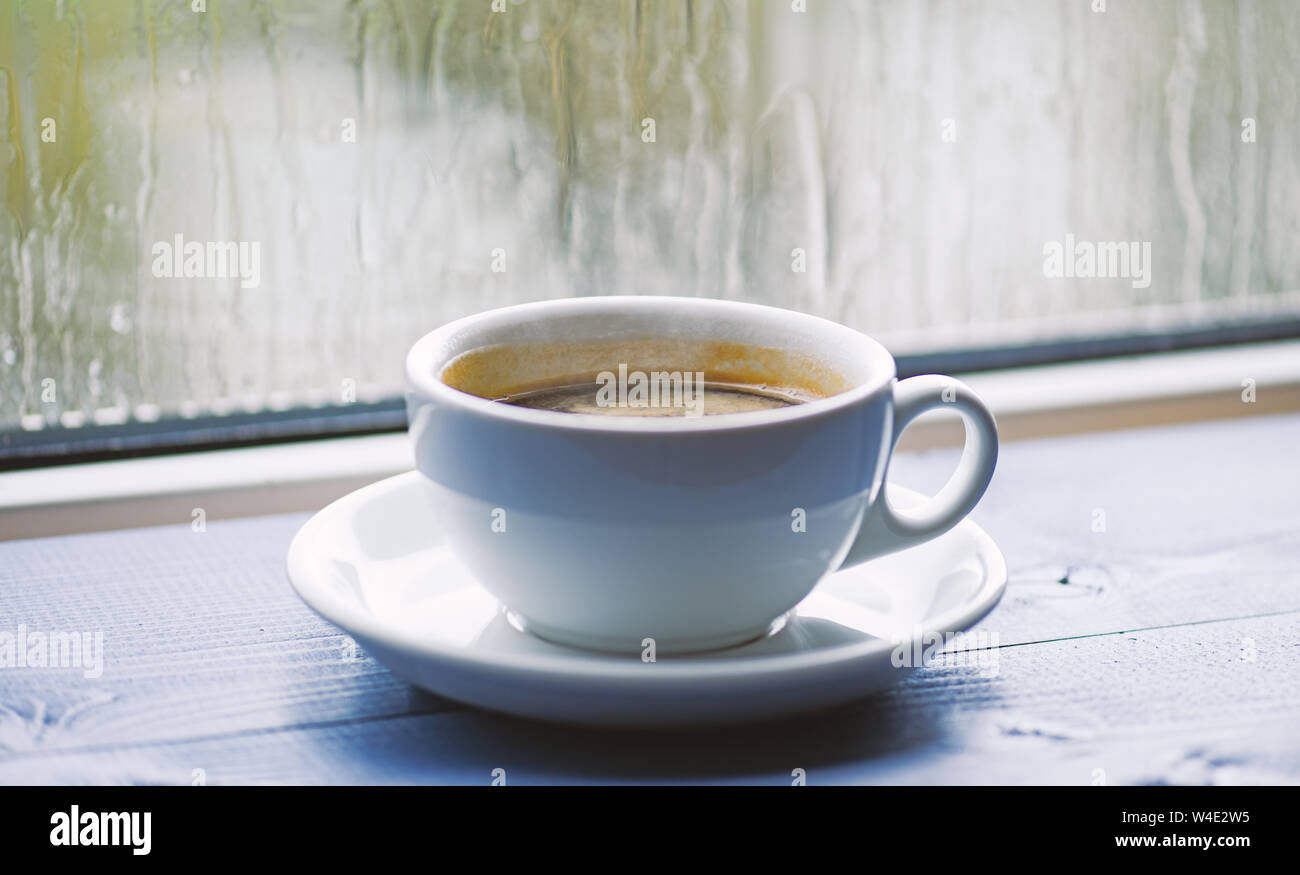 Wet glass window and cup of hot coffee. Autumn cloudy weather better ...