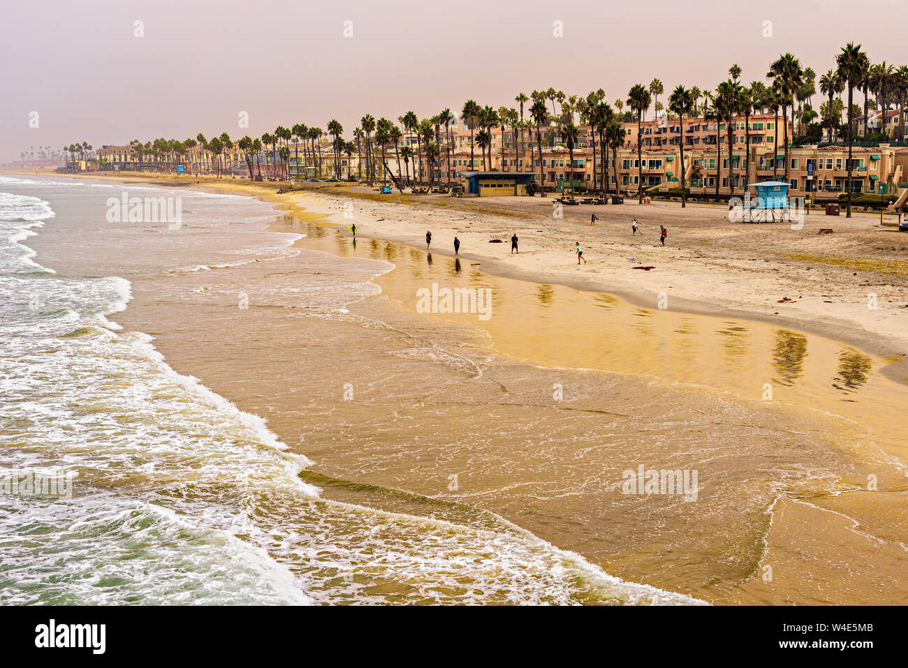 Tourists vacationing on beach, apartments homes, and palm trees line ...