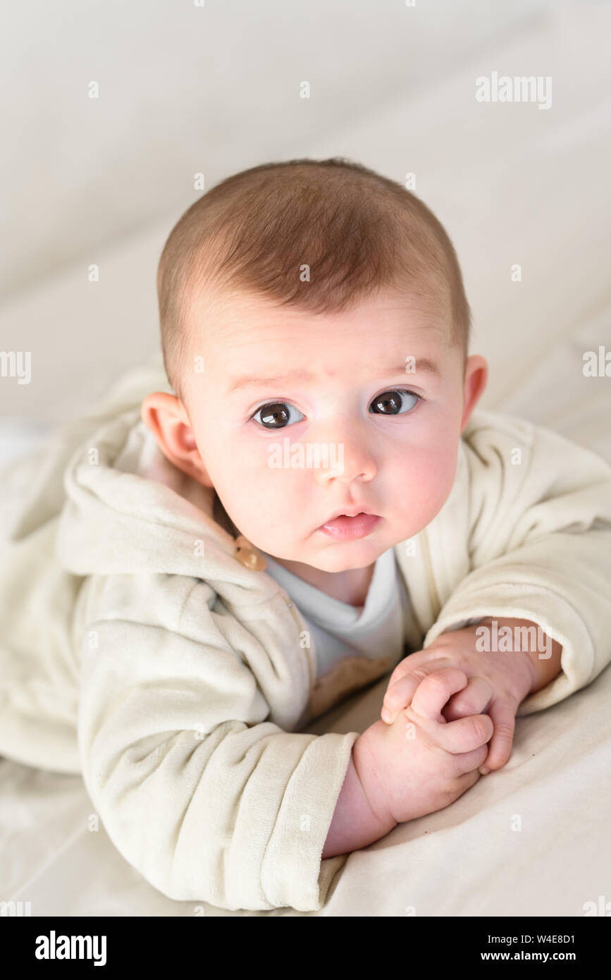 Beautiful and sweet newborn baby lying face down on the bed raising his ...