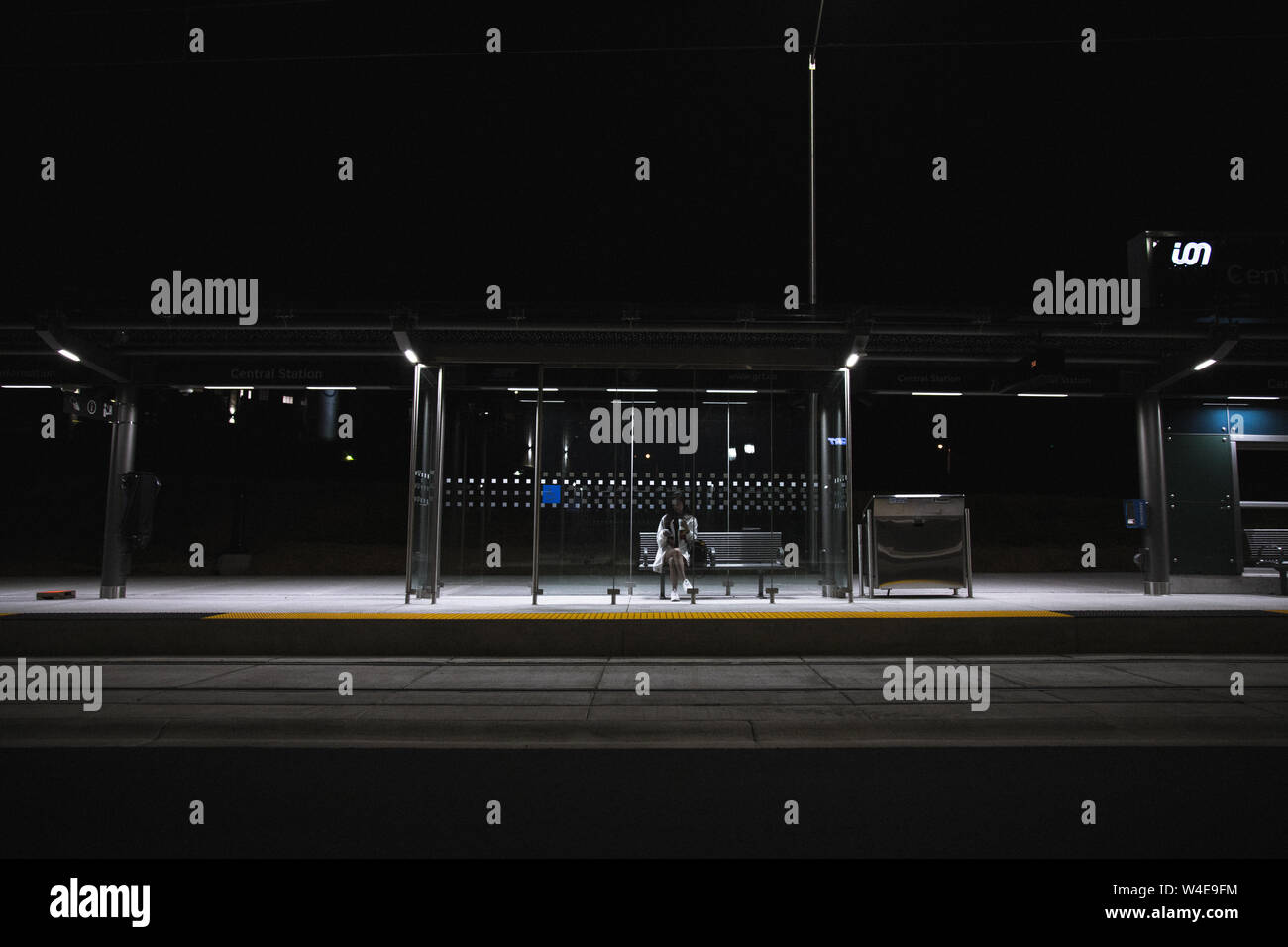 Person sitting alone at a bus stop late at night Stock Photo - Alamy