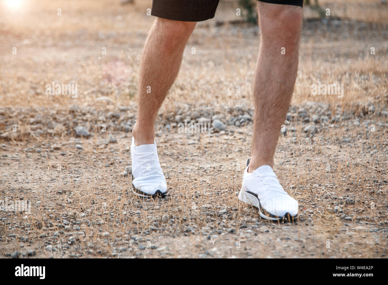men's feet in white sneakers running over rough terrain. Cross country ...
