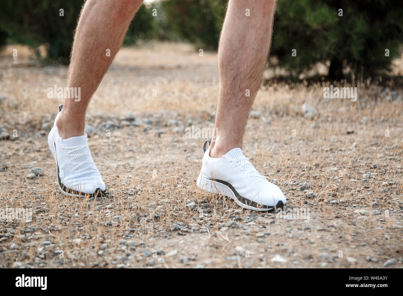 men's feet in white sneakers running over rough terrain. Cross country ...